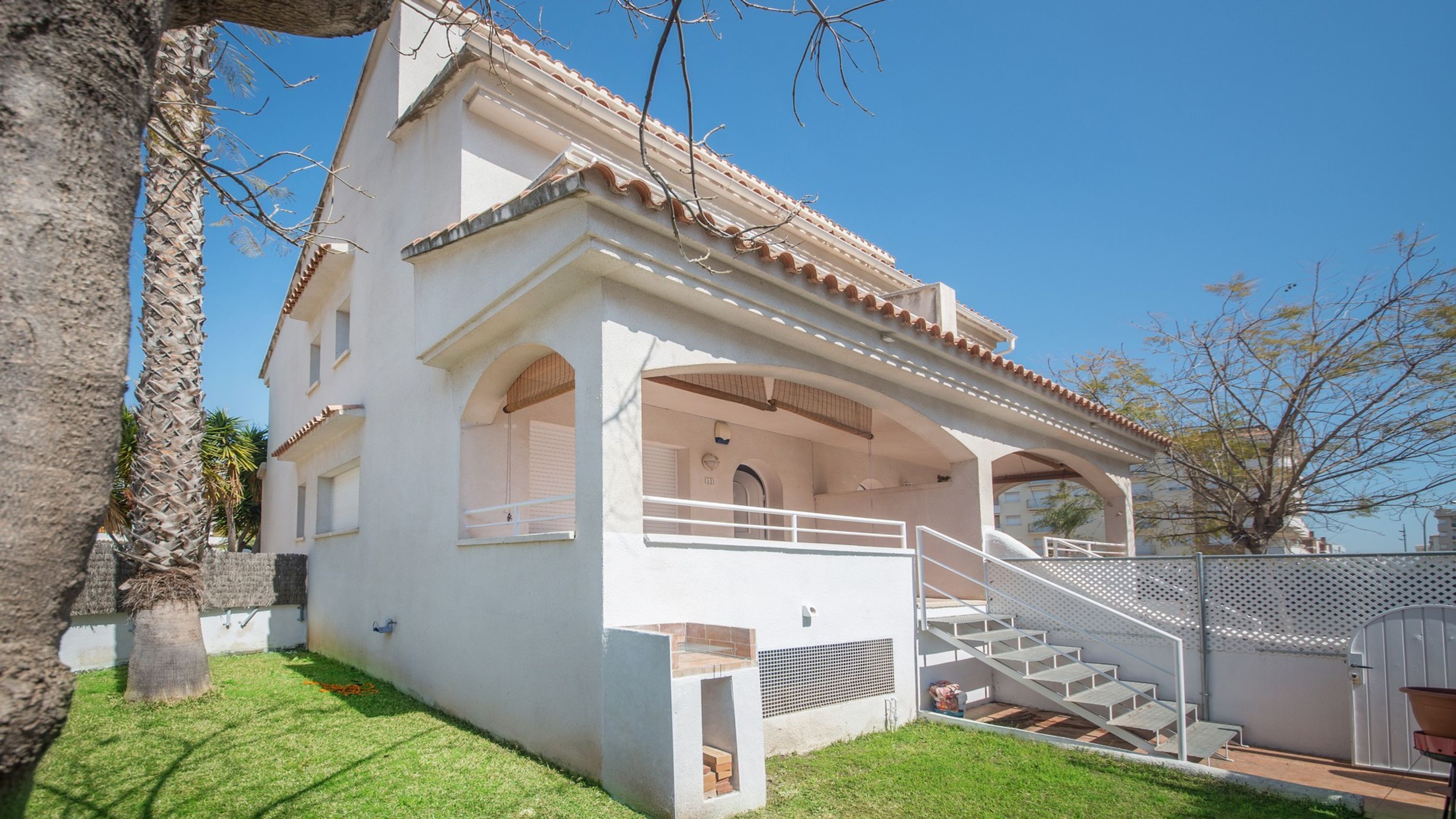 Um edifício branco com telhado cerâmico, uma escadaria que leva a um andar superior e uma pequena área coberta com um banco.