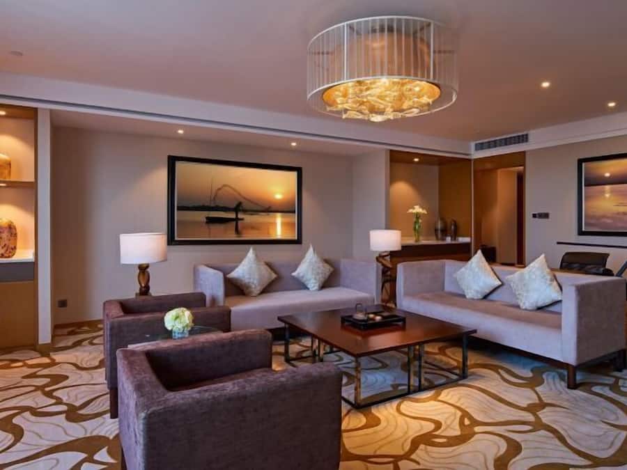 Quarto de hotel moderno com conjunto de sofás, mesa de centro, lustre e obras de arte nas paredes.