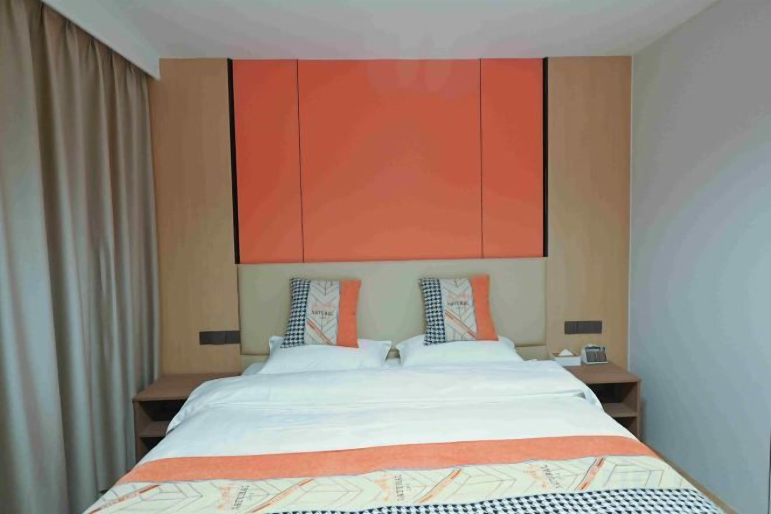 Quarto de hotel com uma cama, uma mesa de cabeceira, um telefone e um armário laranja grande sobre a cama.