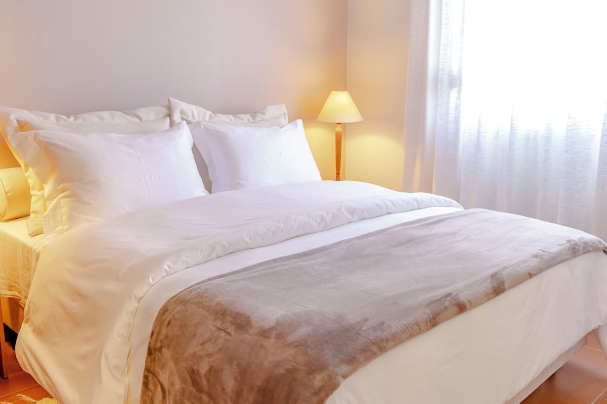 Cama bem arrumada com lençóis brancos e manta marrom.