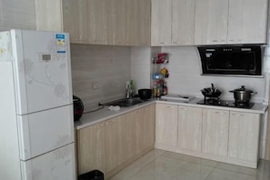 Uma cozinha com armários de madeira clara, uma geladeira branca, um fogão e diversos utensílios de cozinha.