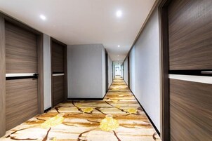 Corredor de hotel com portas de madeira, carpete estampado e um caminho reto que leva a uma saída distante.