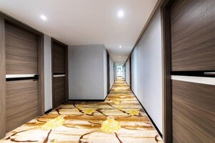 Um corredor de hotel com portas de madeira, carpete estampado e parede em tom claro.