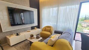 Uma sala de estar moderna com uma grande televisão de tela plana, um sofá, uma poltrona amarela e um espaço de jantar com mesa e cadeiras.