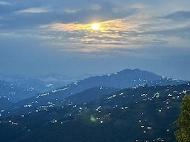 Paisagem montanhosa com luzes dispersas que indicam áreas habitadas, sob um céu crepuscular com o sol se pondo ou nascendo.