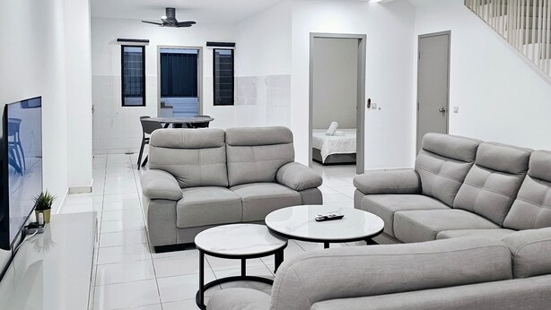 Uma sala de estar moderna com um sofá seccional, uma mesa de centro redonda e uma TV sobre um móvel.