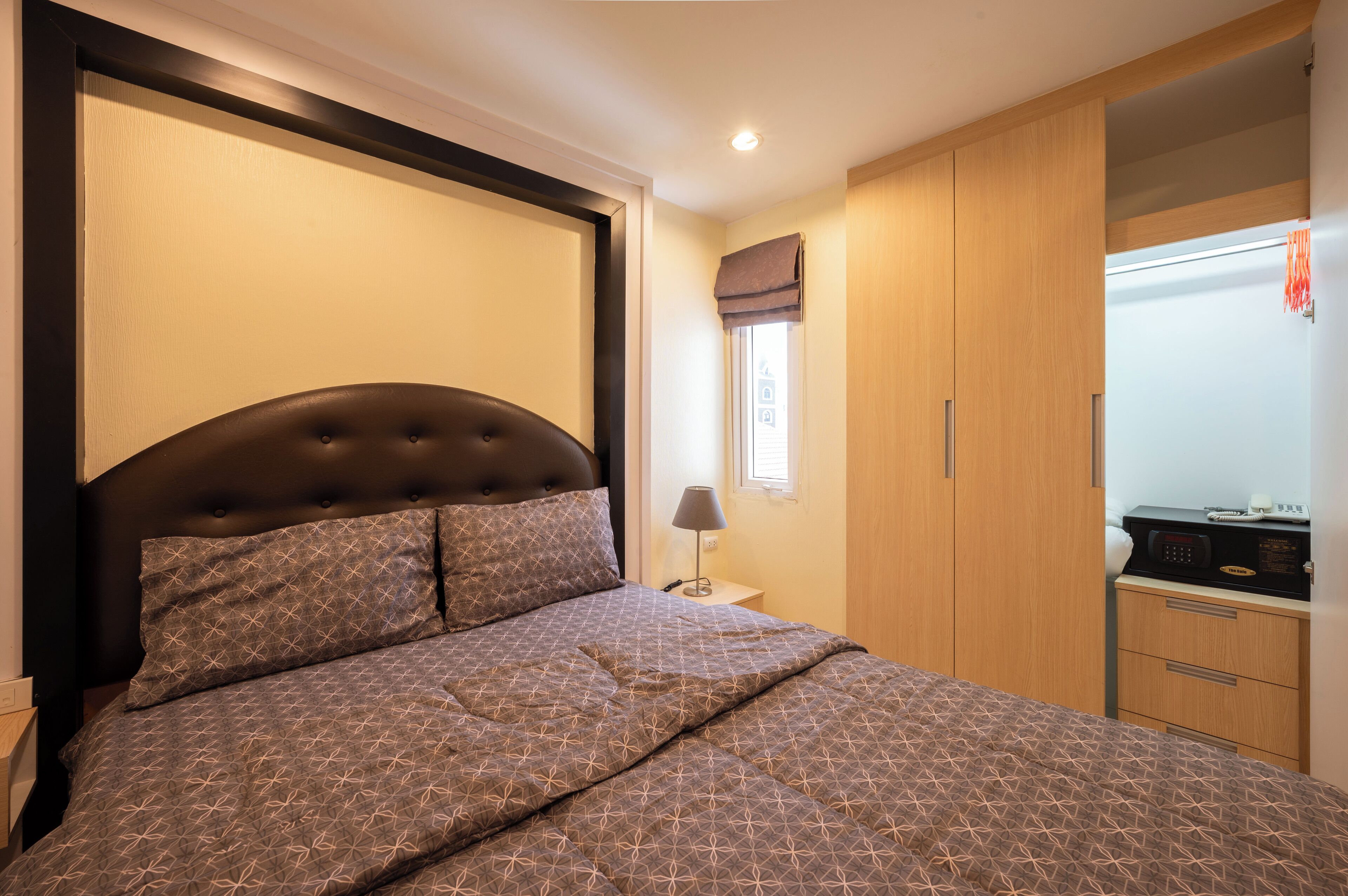 Quarto com uma cama grande, mesa de cabeceira, abajur, guarda-roupa e escrivaninha com um rádio.