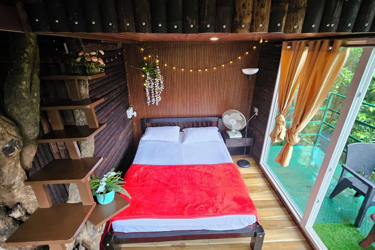 Um quarto acolhedor com uma cama grande, paredes de madeira, uma mesa pequena com uma planta e uma varanda com uma cadeira.