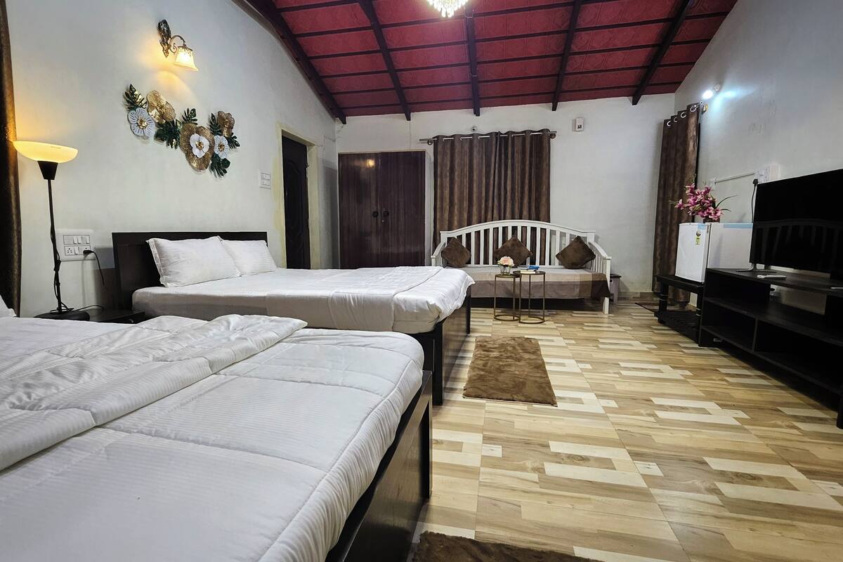 Quarto de hotel com duas camas, televisão, escrivaninha e um objeto decorativo na parede.