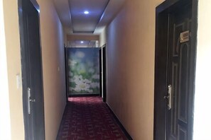 Um corredor com carpete estampado, uma porta com placa e uma parede com um mural floral.