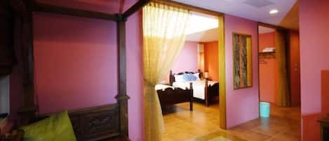 Quarto com uma cama, uma mesa e uma cadeira. Há uma porta que dá para outro cômodo.