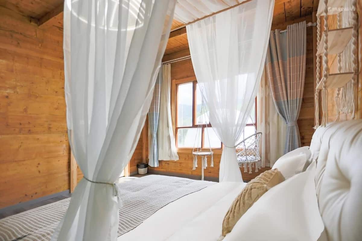 Quarto de cabana de madeira com cama, cortinas brancas e janela.