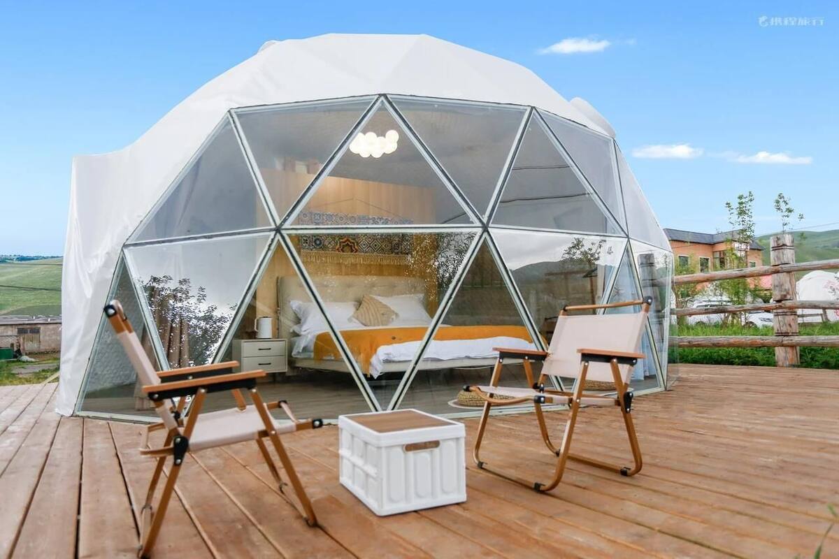 Estrutura em forma de cúpula geodésica com uma cama e área de estar visíveis através das paredes transparentes.