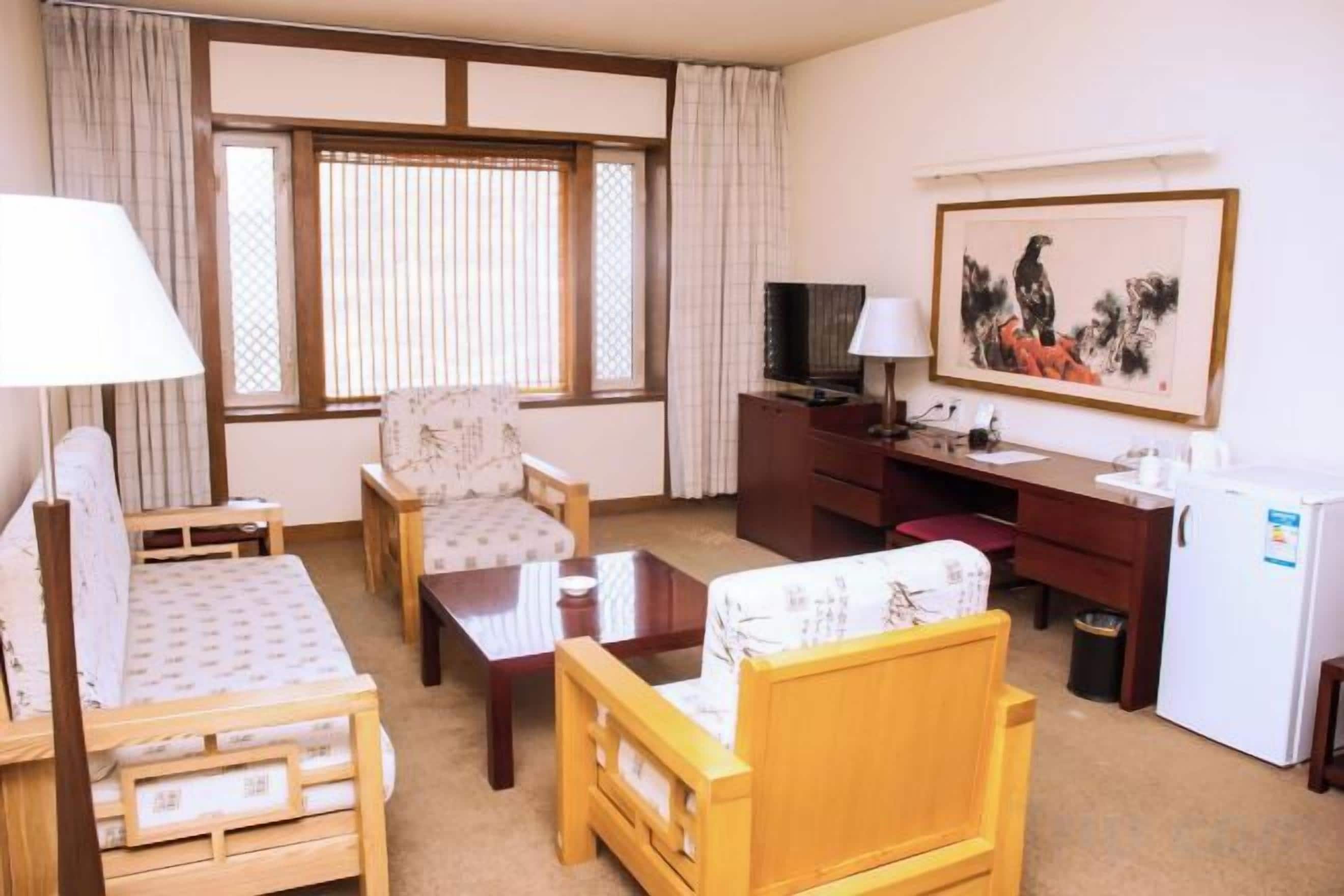Quarto de hotel com cama, escrivaninha, cadeira, televisão e um quadro na parede.