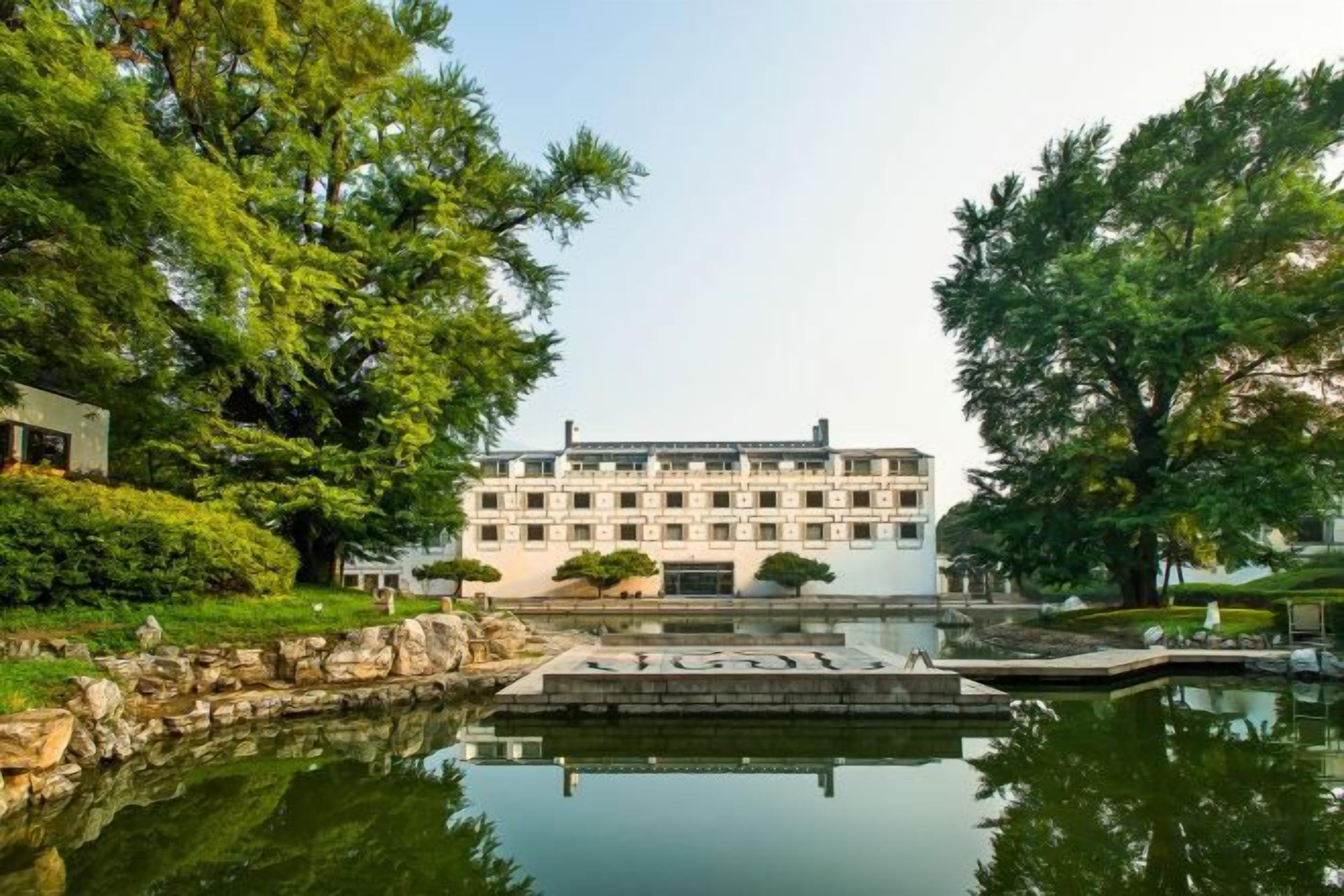 Um edifício refletido em um lago, rodeado por árvores.