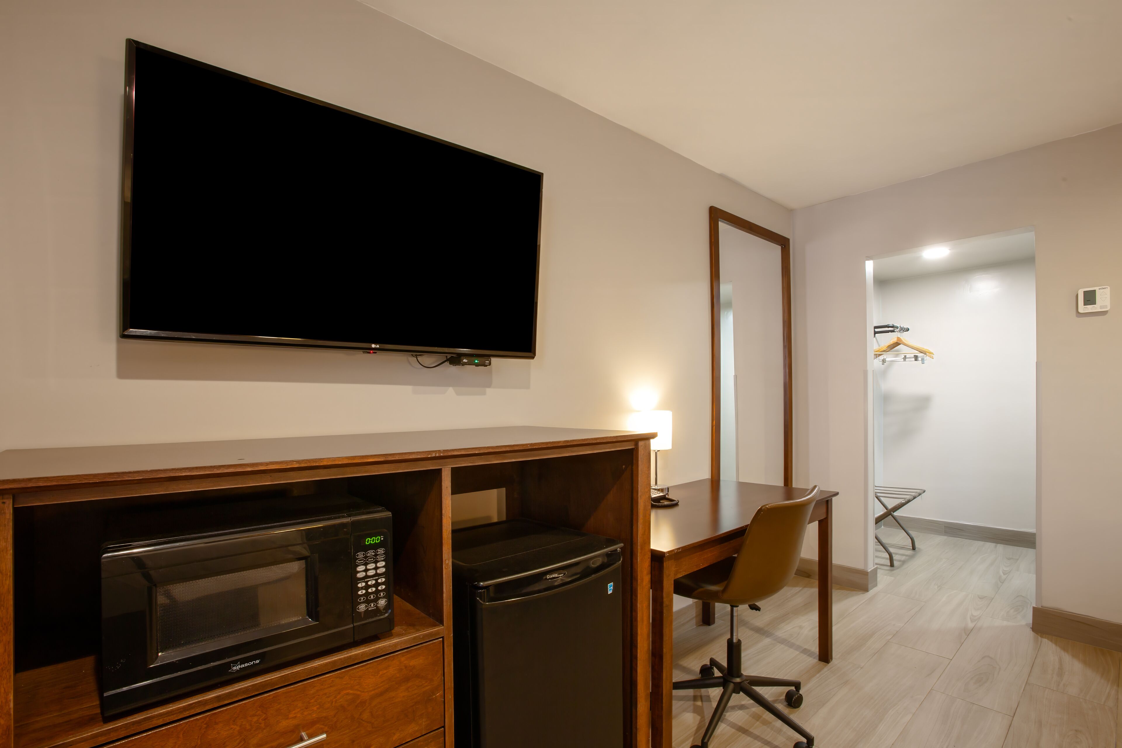Quarto de hotel com televisão de tela plana, micro-ondas, geladeira, escrivaninha e uma cadeira.