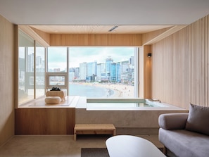 Quarto moderno com uma janela grande com vista para a praia e para a paisagem urbana.