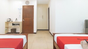 Quarto de hotel com duas camas, guarda-roupa de madeira, um pequeno armário com produtos de higiene e um relógio, e uma televisão.