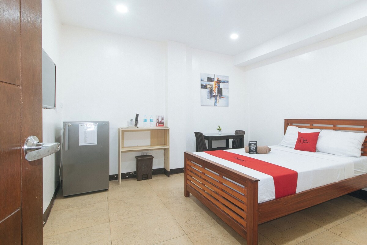 Quarto de hotel com cama de madeira, uma pequena mesa, frigorífico e uma obra de arte na parede.
