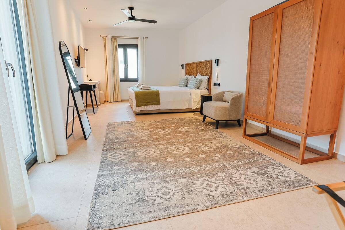 Quarto com cama, mesa de cabeceira e uma janela grande.