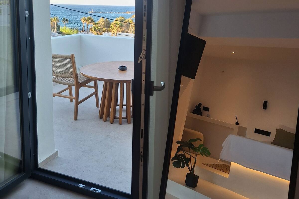 Quarto moderno com varanda, área de refeições com mesa e cadeiras, e cama com planta ao lado.