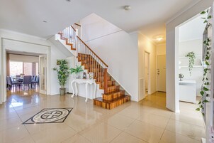 Uma sala ampla com escada de madeira, uma mesa de jantar com cadeiras e um vaso de planta.