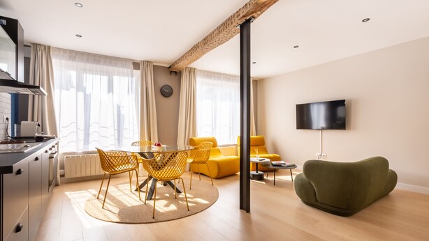Uma sala de estar moderna com área de jantar, sofá, televisão e cozinha.