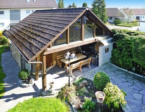 Uma casa com telhado inclinado, deck de madeira e um pátio com mesa e cadeiras.