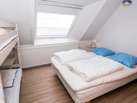 Quarto com beliche, uma cama de solteiro com almofadas azuis, um claraboia e vista para o mar.