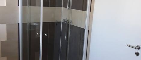 Box de vidro com porta branca e chão ladrilhado.