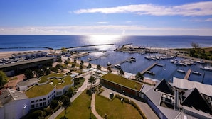 Uma marina com barcos atracados, um cais que se estende na água e edifícios com telhados verdes.