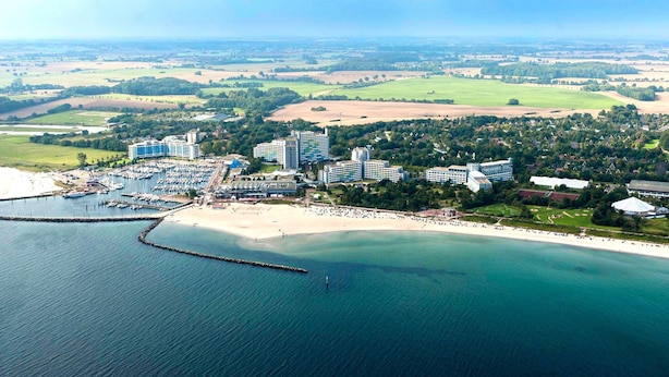 Vista aérea de um hotel à beira-mar com vários edifícios, uma marina e uma praia.