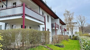 Um edifício residencial com várias andares, varandas, um jardim e céu claro.
