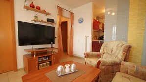 Uma sala de estar com televisão, móvel de entretenimento em madeira, sofá e mesa de centro.