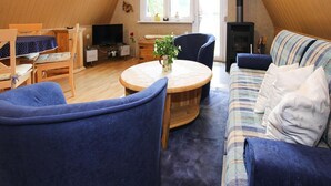 Um quarto de sótão acolhedor, com teto inclinado de madeira, uma mesa de centro redonda de madeira, um sofá azul, uma televisão e uma lareira.