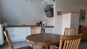 Uma cozinha compacta com armários brancos, uma mesa de madeira redonda e quatro cadeiras de madeira com assentos acolchoados.