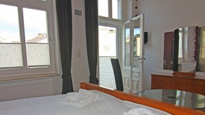 Quarto de hotel com uma cama grande, uma mesa com tampo de vidro, uma cômoda de madeira e um espelho.