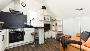 Uma cozinha compacta com forno embutido, uma área de jantar com mesa alta e um espaço de estar com sofá e poltrona.