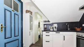 Uma cozinha compacta com armários brancos, bancada preta e porta azul.