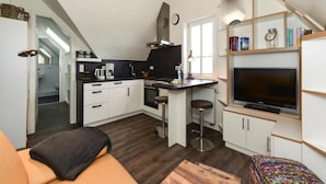 Um espaço compacto com cozinha compacta, sofá, televisão e estante de livros.