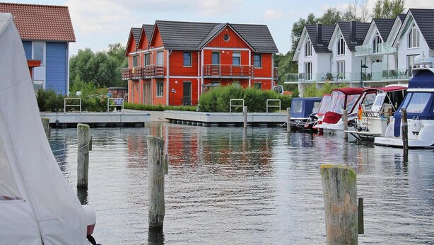 Um canal com barcos, uma casa vermelha e casas brancas.
