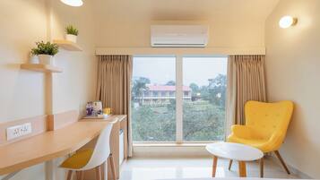 Quarto de hotel moderno com escrivaninha, cadeira amarela e uma janela grande com vista para o exterior.