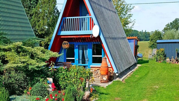 Uma casa com telhado inclinado, varanda frontal azul e um pequeno jardim com flores vermelhas.