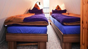 Duas camas beliche de madeira com roupa de cama roxa e laranja num quarto com teto inclinado e janela.