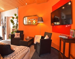 Uma sala de estar moderna com paredes laranja, uma televisão de tela plana, móveis de vime e um espelho grande.