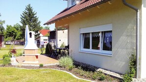 Uma casa residencial com telhado de telhas, varanda coberta com móveis de exterior e um pequeno jardim.