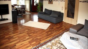 Sala de estar com sofá cinza, piso de madeira, televisão de tela plana e área de jantar com mesa e cadeiras.