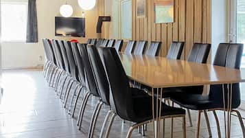 Uma sala de conferências com uma mesa comprida e cadeiras, paredes com painéis de madeira, uma televisão e iluminação pendente.