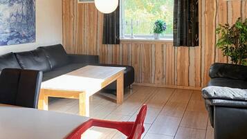 Quarto com parede de madeira, sofá de couro preto, mesa de centro de madeira e janela com cortinas.