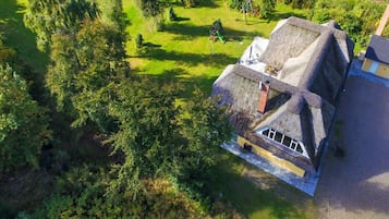 Uma casa com telhado de palha e design inclinado, rodeada por um jardim bem cuidado com diversas plantas e um balanço.